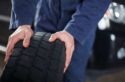 자동차 차고에서 차량 수리를 하기 위해 새 자동차 타이어를 들고 있는 정비사 45 49세에 대한 스톡 사진 및 기타 이미지
