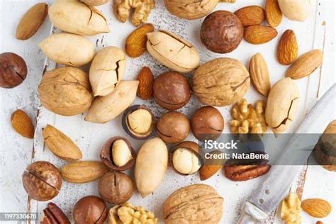 견과류의 혼합 호두 아몬드 피칸 마카다미아와 흰색 나무 도마에 껍질을 여는 칼 건강한 비건 음식 깨끗한 식사 균형 잡힌 식단 상단 보기 매크로 닫기 0명에 대한 스톡 사진