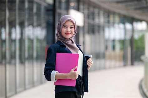 히잡을 쓴 젊은 무슬림 여성 사업가가 디지털 태블릿과 서류 뭉치를 들고 현대식 사무실 건물 앞에 서 있다 20 24세에 대한 스톡 사진 및 기타 이미지 Istock