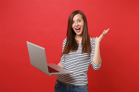 흥분 젊은 여 자가 입 벌리고 찾고 손에 붉은 배경에 고립 된 노트북 Pc 컴퓨터에서 작업을 확산 사람들이 진심으 감정 라이프 스타일 개념 복사 공간을 비웃는 다 갈색