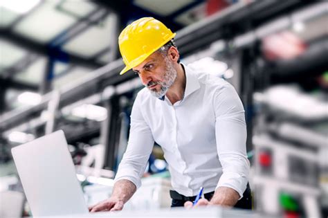 현대 산업 공장에서 컴퓨터 옆에 서서 전화를 거는 관리자 로봇 공학 로봇 팔 및 자동화를 갖춘 제조 시설 창고에 제품 및 자재