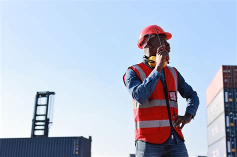 워키토키 무선 제어 적재 컨테이너 상자를 사용하는 감독 엔지니어 컨테이너 화물 현장에서 헬멧 작업을 통한 자신감 있는 엔지니어링 및 산업용 컨테이너 화물 운송 선박 점검