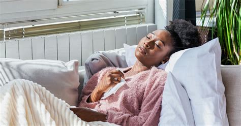 질병 계절성 바이러스 문제 개념 독감에 걸린 여자가 소파에 누워 온도계의 온도를 보고 있다 고열로 침대에 누워있는 아픈 여자 감기 독감과 편두통 사진