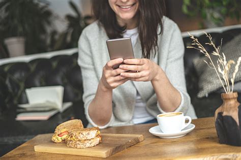 레스토랑에서 로프트 인테리어 공간 안에 인식할 수 없는 여자 사람 사진을 잘립니다 그녀는 안락의 자에 앉아 하 고 미소로 휴대용 전화 장비에 표시를 보고 휴식에 대한 스톡