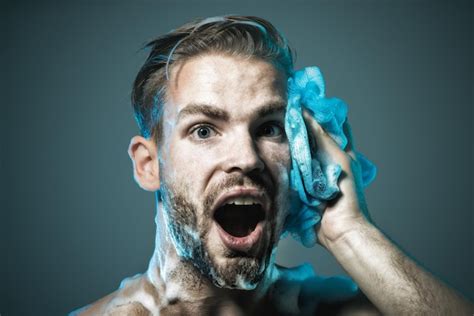 스폰지로 몸을 씻는 잘생긴 근육질의 남자 벌거 벗은 남자 젖은 몸과 얼굴 젊은 남자는 샤워에서 씻는다 비누 스폰지로