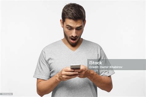 그녀의 스마트폰 회색 배경에 고립의 디스플레이에 웹에서 미디어 콘텐츠 감동된 젊은 남자의 초상화 충격 콘텐츠 개념 T 셔츠에 대한 스톡 사진 및 기타 이미지 Istock