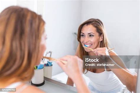 매력적인 여성의 초상화는 욕실에서 양치질을하고 반사에 거울을보고 건강한 치아 행복한 사랑스러운 젊은 여자 보고 거울과 양치질 이빨 에 욕실 가정 생활에 대한 스톡 사진 및