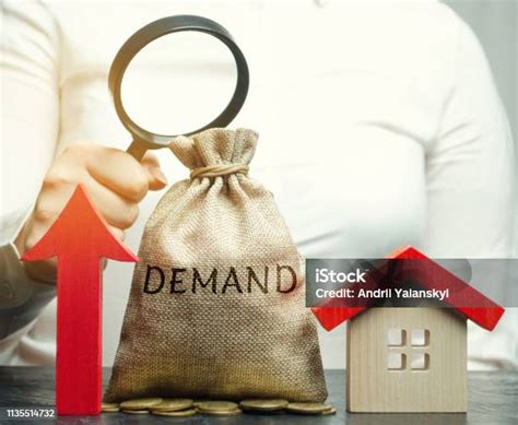여성의 손은 단어 수요 위쪽 화살표와 집과 돈 가방에 돋보기를 들고 있다 부동산에 대 한 높은 수요의 개념 모기지 및 주택 구매에 대 한 관심 증가 가격에 대한 스톡 사진