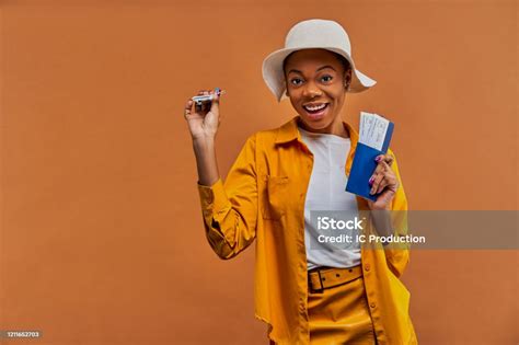 노란 셔츠를 입은 흰색 모자를 쓴 여성이 티켓을 손에 들고 있는 장난감 비행기를 들고 카메라를 바라보며 미소짓고 있다 여행 컨셉 아프리카 민족에 대한 스톡 사진 및 기타
