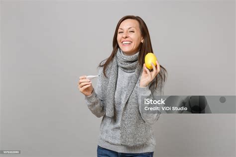 스튜디오에서 회색 벽 바탕에 회색 스웨터 스카프 레몬 온도계를 들고 웃는 젊은 여자 고립 건강 한 생활 습관 병 아픈 질병 치료 추운 계절 개념 복사 공간을 비웃는 다