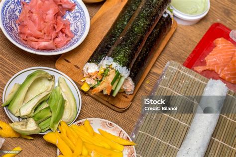 집에서 초밥과 롤 만들기 일본 전통 음식의 재료로 접시를 만들고 부엌 테이블에 있는 나무 판에 스시 롤을 올려놓고 위에서 바라볼 수 있습니다 고급 요리에 대한 스톡 사진 및