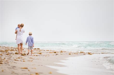 바다 해변을 따라 걷는 그녀의 두 어린 소년과 흰색 드레스를 입은 젊은 어머니 바다에서 휴가를 즐기는 아기와 소년과 여자 빈 해변에서 어머니 가족에 대한 스톡 사진 및 기타