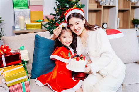 예쁜 엄마와 귀여운 딸이 집의 소파에 앉아 선물 상자를 들고 기쁜 듯이 웃고 있다 생일 케이크와 장식된 크리스마스 트리가 축제 분위기를 더합니다 12월에 대한 스톡 사진 및