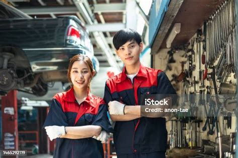 아시아 자동차 엔지니어 사람들은 정비사 차고에서 헬멧 작업을 착용합니다제복을 입은 젊은 자동차 정비사는 카메라를 보고 웃으며 차를 검사하고 있습니다 수리에 대한 스톡 사진