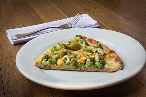 브로콜리 피자는 나무 판에 제공됩니다 모짜렐라 브로콜리 옥수수 완두콩 올리브로 구운 제품입니다 접시에 담긴 피자 조각 포크와 칼 미식 사진입니다 길거리 음식에 대한 스톡