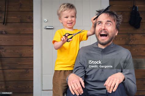 검역 잠금 중에 집에서 아버지에게 머리카락을 자르는 재미있는 아이 작은 미용사 이발사는 그의 무서운 수염 아빠에 이발을합니다 홈 라이프 스타일 컨셉에서 아름다움과 자기 관리