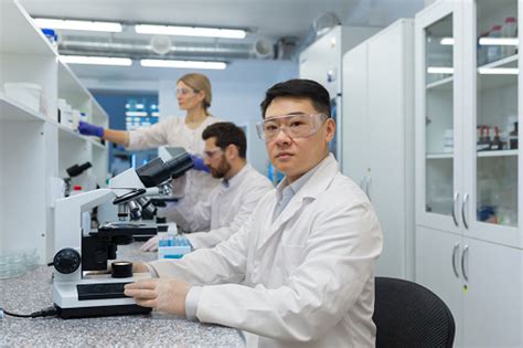 젊은 의대생과 과학자 그룹이 대학의 실험실에서 공부하고 있습니다 아시아 청년이 현미경 뒤에 앉아 카메라를 진지하게 바라보고 있습니다 과학자에 대한 스톡 사진 및 기타 이미지