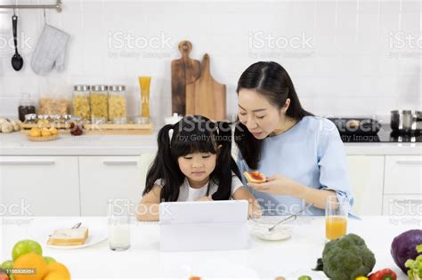 행복한 아시아 가족 어머니와 어린 소녀는 아침 식사 우유와 시리얼 잼빵을 먹고 집에서 부엌에서 디지털 태블릿을 참조하십시오 건강한 음식과 아침 활동 2명에 대한 스톡 사진