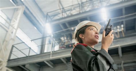 현대 공장의 대규모 작업장에 서 있는 동안 워키토키를 사용하는 보호 헬멧과 작업복을 입은 젊은 여성 엔지니어 사진 Unsplash의 사진술 이미지