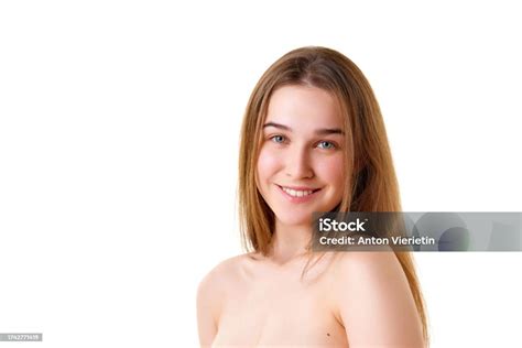 벌거벗은 어깨와 반짝이는 긴 갈색 머리를 가진 매력적인 소녀의 초상화는 하얀 스튜디오 배경에 카메라를 바라보며 이빨을 드러내며 웃고 있다 18 19세에 대한 스톡 사진 및