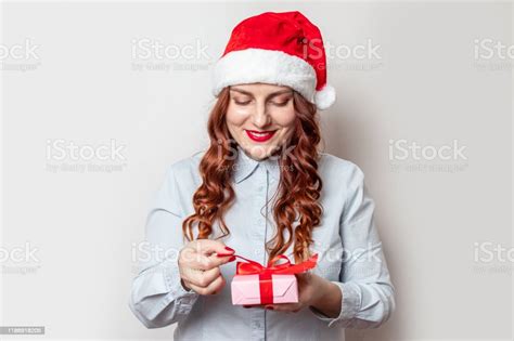 곱슬 머리와 그녀의 머리에 빨간 산타 모자와 만족 어린 소녀는 선물 상자를 들고 회색 벽에 미소 겨울에 대한 스톡 사진 및 기타 이미지 Istock