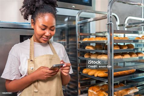 카메라를 보는 아프리카 계 미국인 여성 빵 굽는 사람 요리사 드레스와 모자를 쓰고 부엌에서 함께 요리하는 요리사 베이커 그녀는 부엌의 현대 전기 오븐에서 신선한 구운 쿠키를