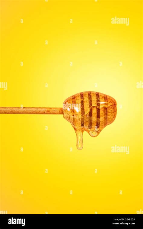 A Vertical Shot Of Appetizing Honey Flowing From A Wooden Dipper Isolated On Bright Yellow