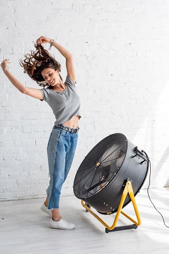 불어 전기 인공 호흡기 앞에서 손을 들고 서있는 파란색 청바지에 예쁜 행복한 여자 선풍기 전기 설비에 대한 스톡 사진 및 기타 이미지 선풍기 전기 설비 열 개념