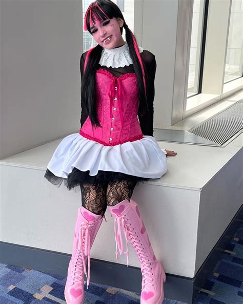 A Woman Dressed In Pink And Black Sitting On A Ledge
