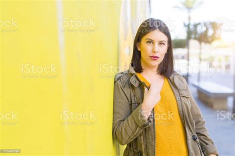 화창한 날에 도시의 거리를 걷고 노란색 벽에 기대어 자신감과 쾌활한 미소 아름다운 젊은 여성 갈색 머리에 대한 스톡 사진 및 기타 이미지 Istock