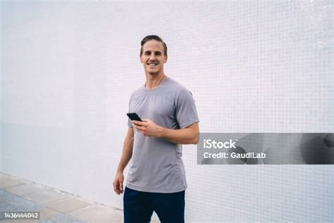 운동에 대한 미디어 콘텐츠를 공유하기 위해 휴대 전화를 사용하는 활동복을 입은 쾌활한 남성 조깅하는 사람의 절반 길이 초상화 거리에서 스마트폰을 들고 카메라를 보고 있는