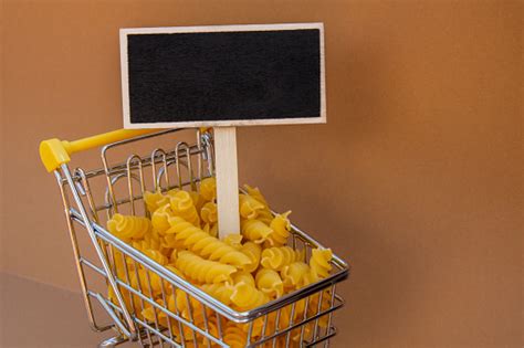 빈 모형 템플릿 쇼핑 트롤리 카트에 대한 칠판 레이블 베이지색 배경에 파스타로 가득 차 있습니다 텍스트를위한 공간을 복사하십시오 식품 및 식료품 쇼핑 가격 인상 식량 비용