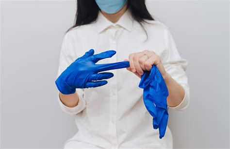 흰색 코트와 보호 의료 마스크를 착용한 젊은 여성 의사는 라텍스 고무 장갑을 벗습니다 코로나 바이러스에 대한 싸움의 개념