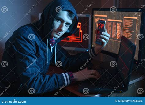Hacker In The Hood Holding The Phone In His Hands Trying To Hack The Mobile Device Cloud The