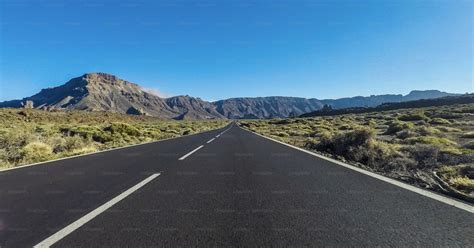 앞에 벌컨 마운트가 있고 푸른 맑은 하늘이 있는 산의 장거리 도로 검은색 아스팔트와 흰색 선이 있는 지상 관점 운전 및 여행 개념 사진 Unsplash의 구분선