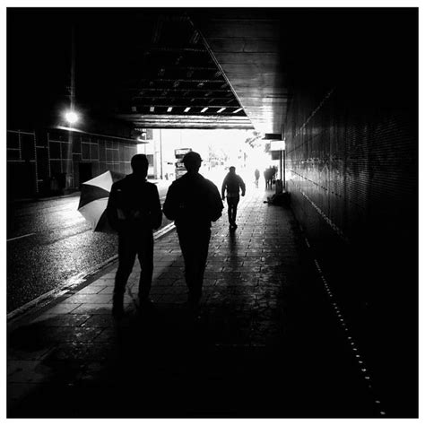 Two Men Walking Down A Dark Tunnel Holding Umbrellas