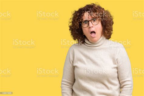 아름 다운 중간 어른 수석 입고 여자 터틀 넥 스웨터와 안경 충격 얼굴에 고립 된 배경 위에 보고 회의 냉소 오픈 입으로 놀