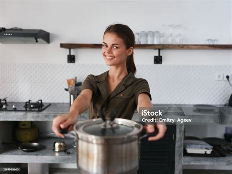 스타일리시한 부엌에서 음식을 준비하고 저녁 식사를 준비하기 위해 손에 냄비를 들고 카메라를 카메라에 담은 채 이를 악물고 미소를 지으며 카메라를 바라보고 있다 가정 분위기