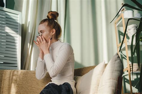 소파에 앉아 집에서 미용 시술을 즐기며 얼굴에 하얀 안면 시트 마스크를 바르는 아름다운 젊은 여성 얼굴 피부 관리 테라피 트리트먼트 뷰티 스킨 케어 여자는 스킨 케어