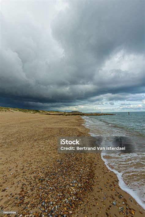모래 언덕을 따라 장엄한 모래와 돌해변의 전경과 바위 그로인이 있는 잔잔한 물과 검은 구름이 있는 폭풍우가 몰아치는 하늘 아래 언덕을 배경으로 펼쳐지는 풍경 0명에 대한