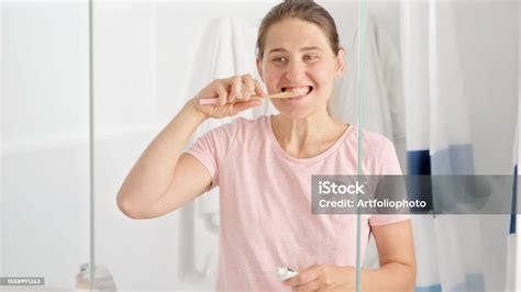 젊은 갈색 머리 여자는 화장실에서 거울 앞에 서서 나무 칫솔로 이를 닦고 있다 치아 건강 자가 점검 입 및 구강 위생의 개념 30 34세에 대한 스톡 사진 및 기타 이미지