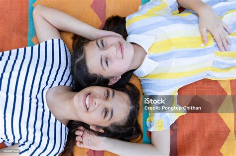 밝고 화려한 바닥 옷을 입고 누워있는 동안 두 소녀 어린이가 머리 뒤에서 손을 잡고 미소를 짓는 모습 즐기고 카메라를보고 친구와 우정 개념 누워있기에 대한 스톡 사진 및