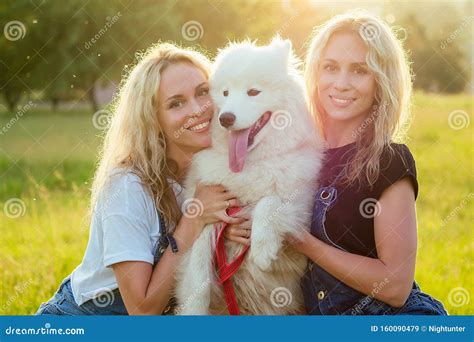 Two Beautiful And Charming Curly Blonde Twins Smiling Toothy Woman In Denim Overalls Are Sitting