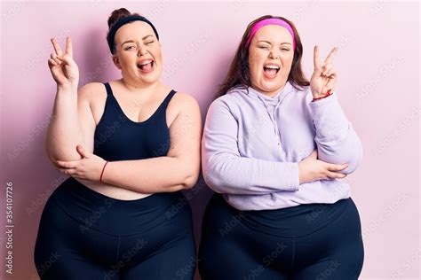 Young Plus Size Twins Wearing Sportswear Smiling With Happy Face Winking At The Camera Doing