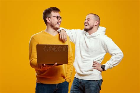 Two Funny Friends Men In Yellow Sweater And White Hoodie Working On Laptop Computer And Smiling