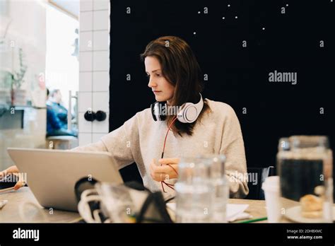 Young Female Computer Programmer With Headphones Working While Sitting At Desk In Small Office