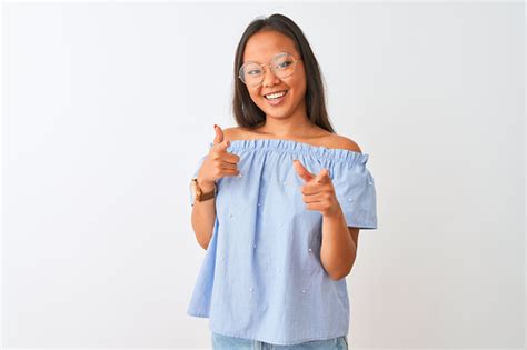 행복하고 재미있는 얼굴로 카메라에 손가락을 가리키는 고립 된 흰색 배경 위에 파란색 티셔츠와 안경을 착용한 젊은 중국 여성 좋은 에너지와 분위기 T 셔츠에 대한 스톡 사진