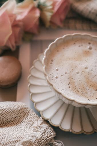 무채색 패브릭 배경에 거품 커피 한 잔 분홍색 마카롱 부드러운 분홍색 장미를 놓고 평평하게 누워 있습니다 파스텔과 베이지 톤의 우아하고 아늑한 구성 감정에 대한 스톡 사진