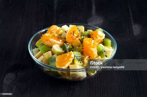 유리 그릇에 과일 샐러드를 닫습니다 상쾌한 과일 샐러드 나무 테이블에 녹색 민트와 건강한 샐러드 검은 색 배경에 신선한 바나나 오렌지 키위를 혼합합니다 복사 공간을