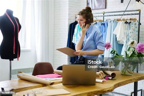 쇼룸에서 모바일 대화 테일러링 의류를 작업하는 집중 여성 드레스 메이커 스튜디오에서 현대 기술을 사용하여 새로운 컬렉션을 생산하기위한 전문 쿠튀리에 예약 섬유 공예에 대한